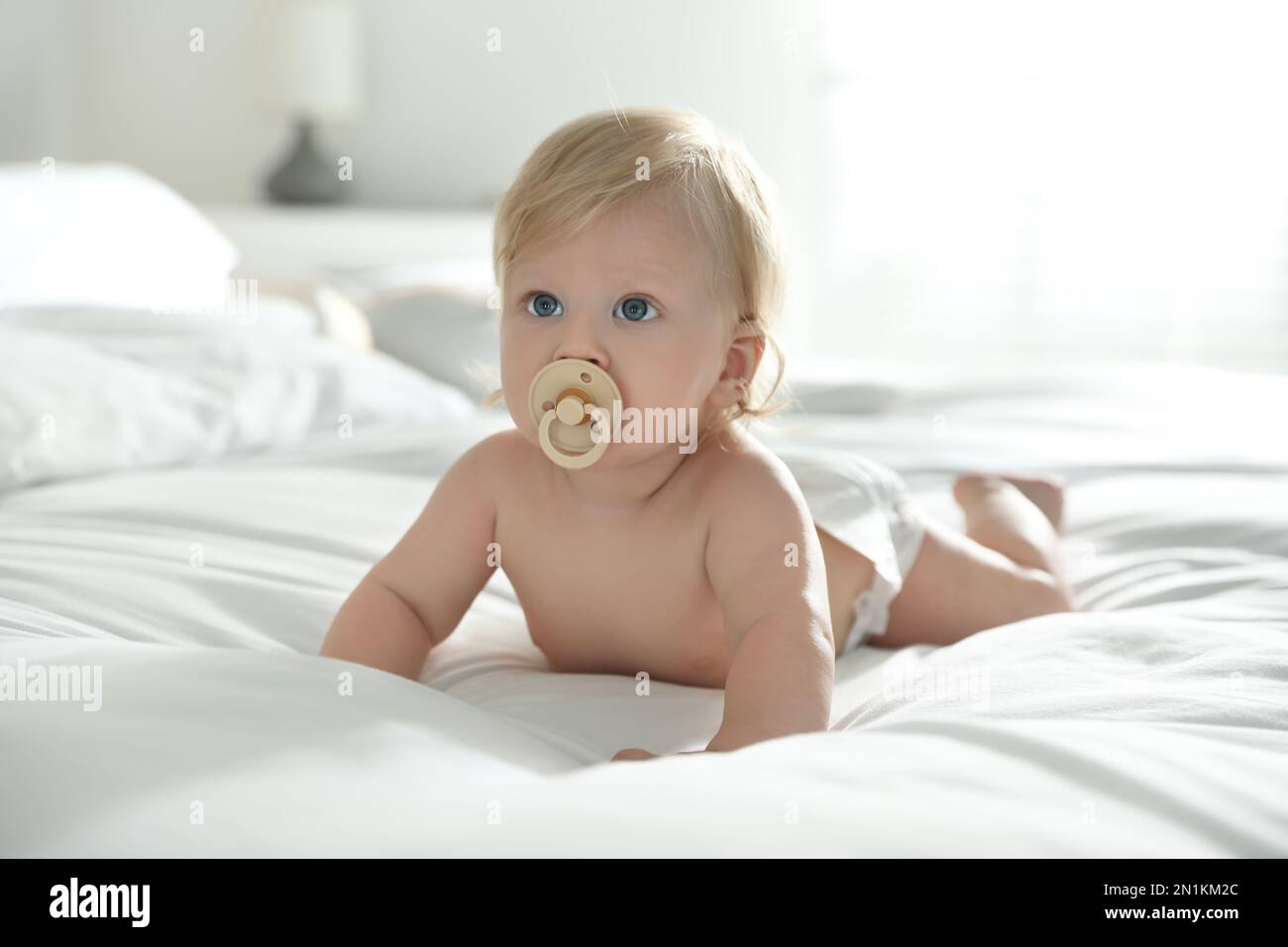 Cute little baby in diaper with pacifier lying on bed at home Stock ...