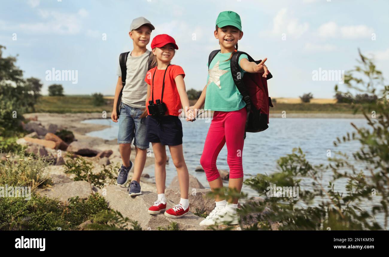 Cute little children with backpacks and binoculars on rock near river ...