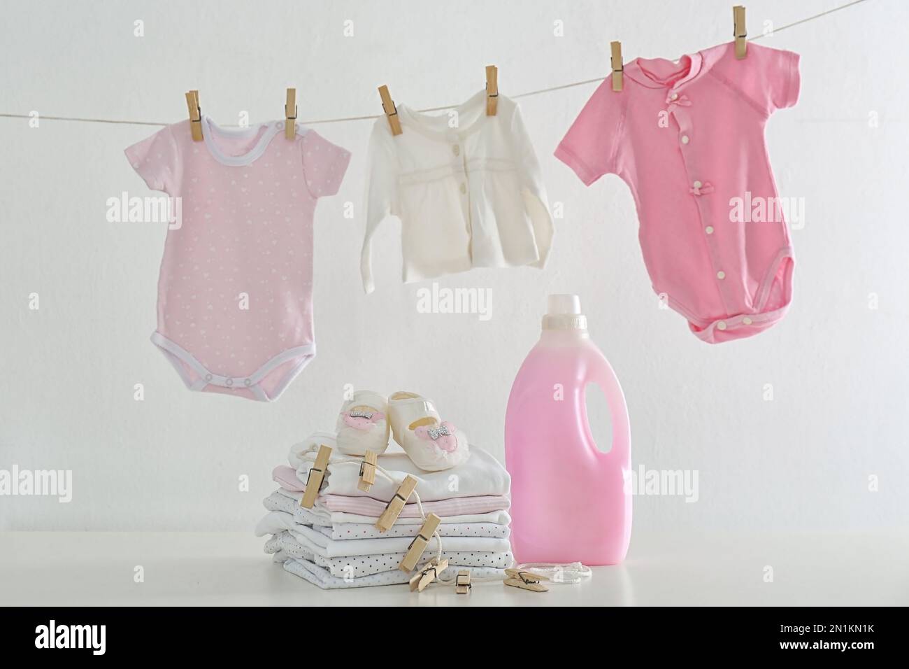 Fresh baby laundry hanging on clothesline and bottle of detergent on ...