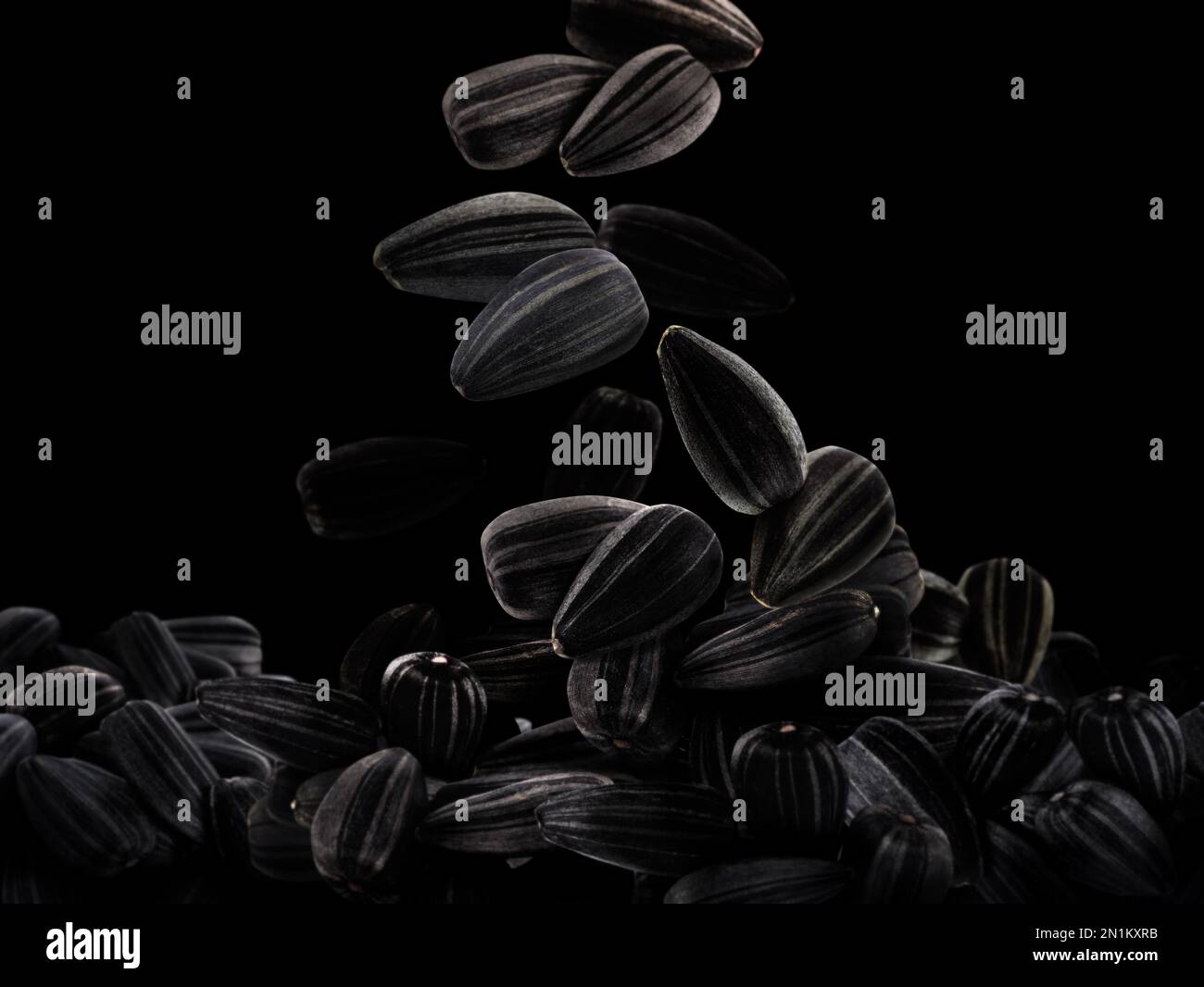 Sunflower seeds falling onto heap on black background Stock Photo - Alamy