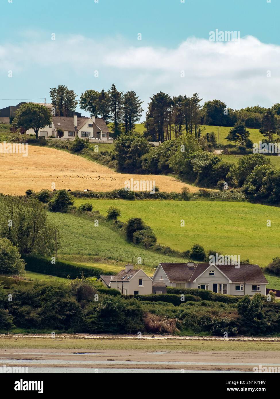 Several buildings and trees on a green hill. Irish summer landscape ...