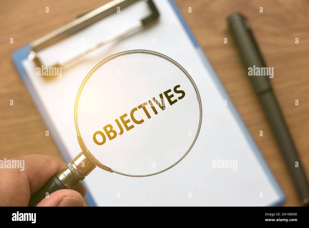 A hand magnifying a words of Objectives from a white paper using ...