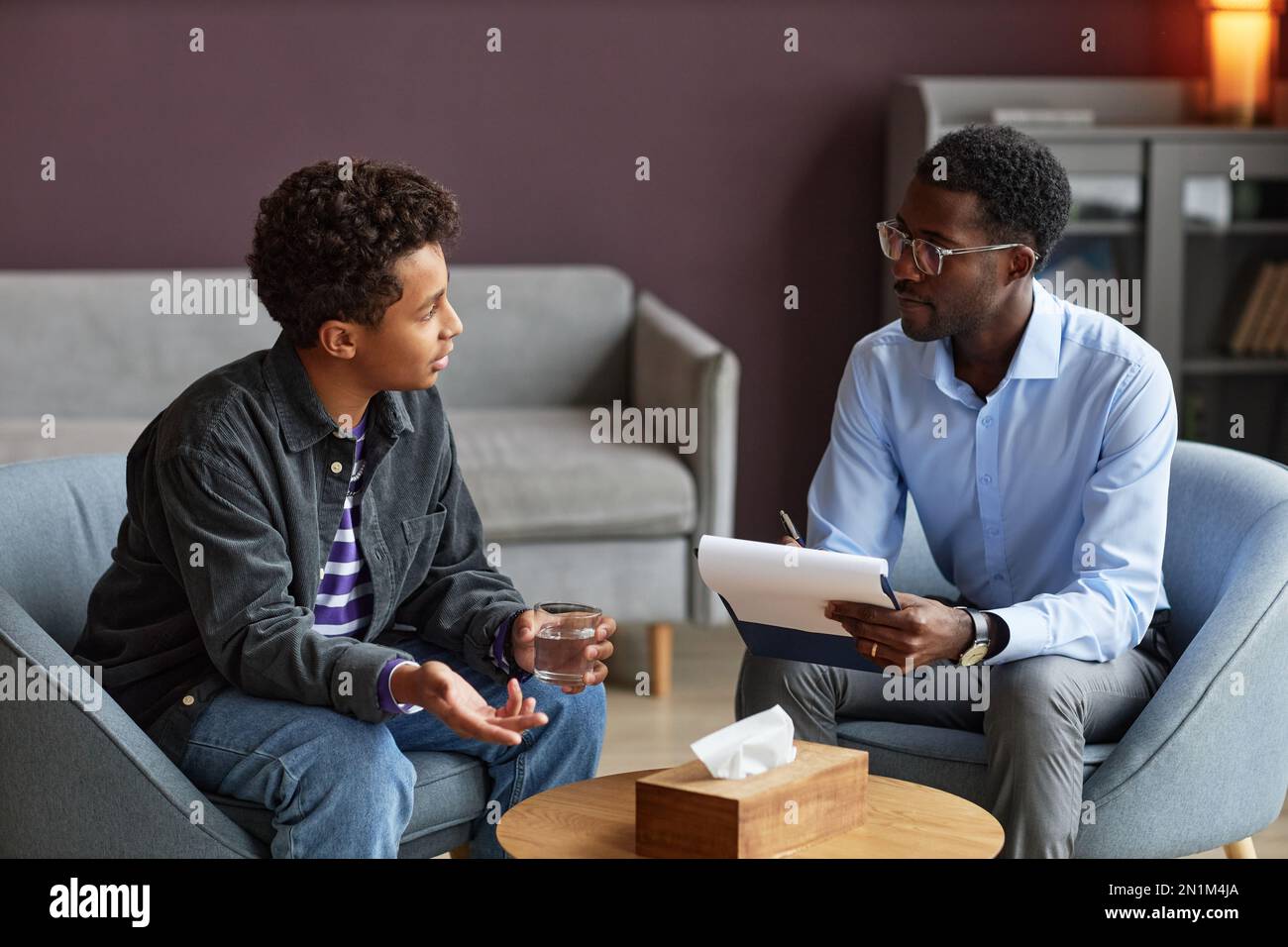 Teenage boy drinking water when talking to adolescent psychologist ...