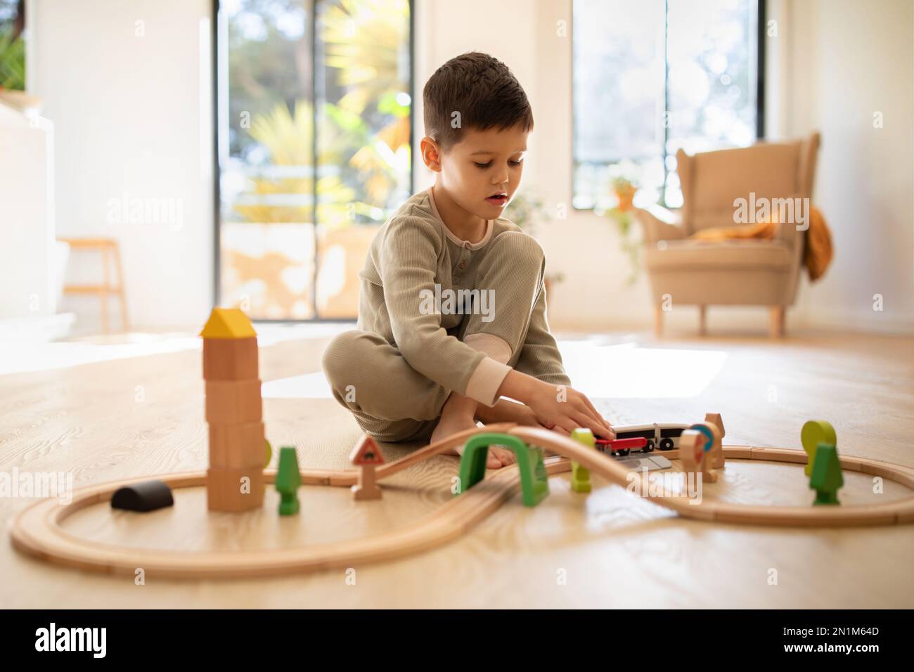 Busy serious caucasian little kid builds city, plays wooden road, train ...