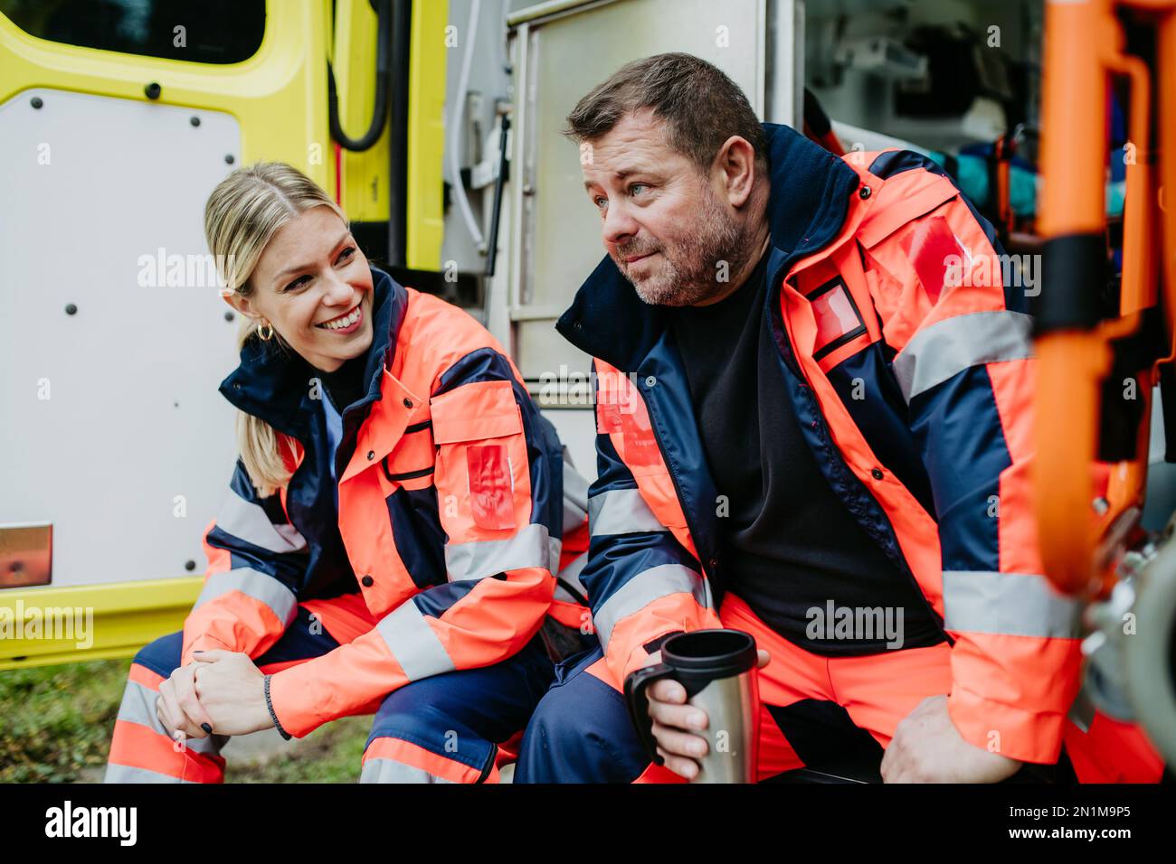 Rescuers having break in front of ambulance car, talking and drinking ...