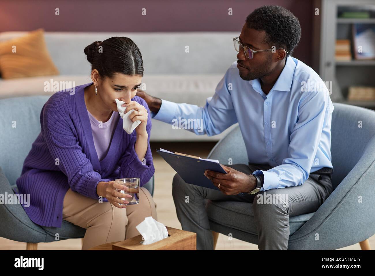 Psychologist reassuring crying young woman drinking water and wiping ...