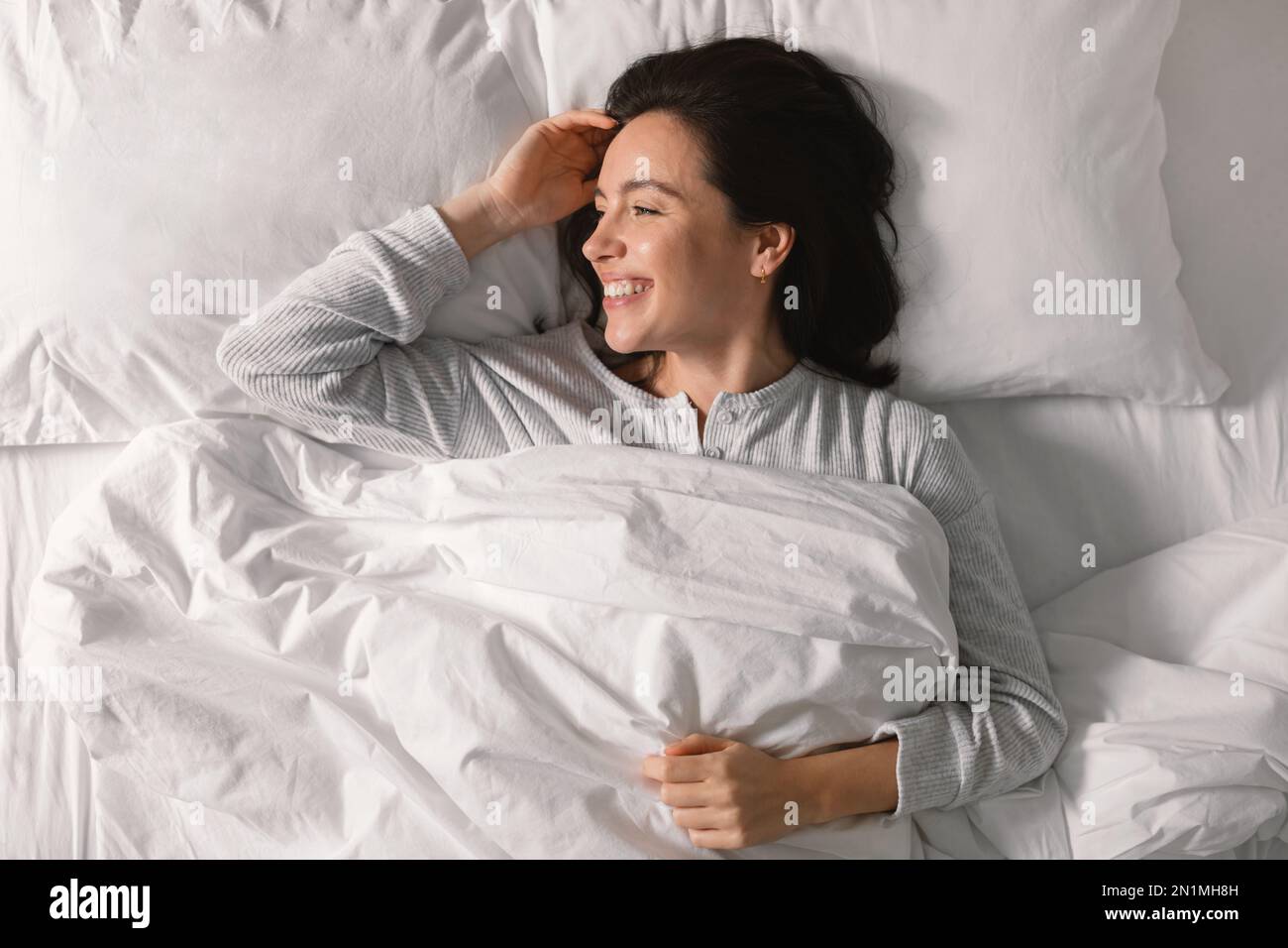 Cheerful pretty young european lady sleeping on white bed, waking up ...