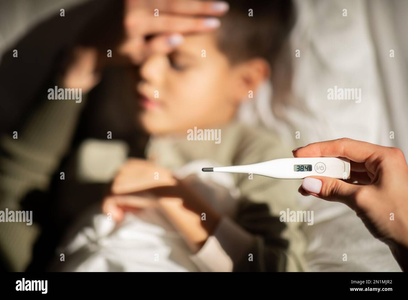 Unhappy caucasian little child suffers from fever, mom measures temperature, show thermometer ...