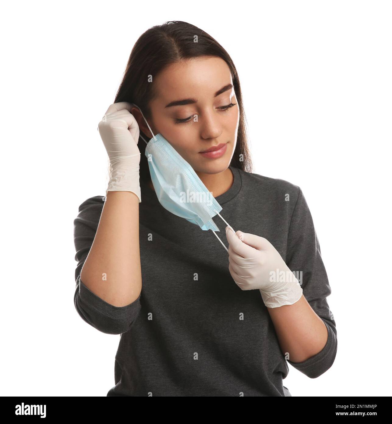 Woman in medical gloves putting on protective face mask against white ...