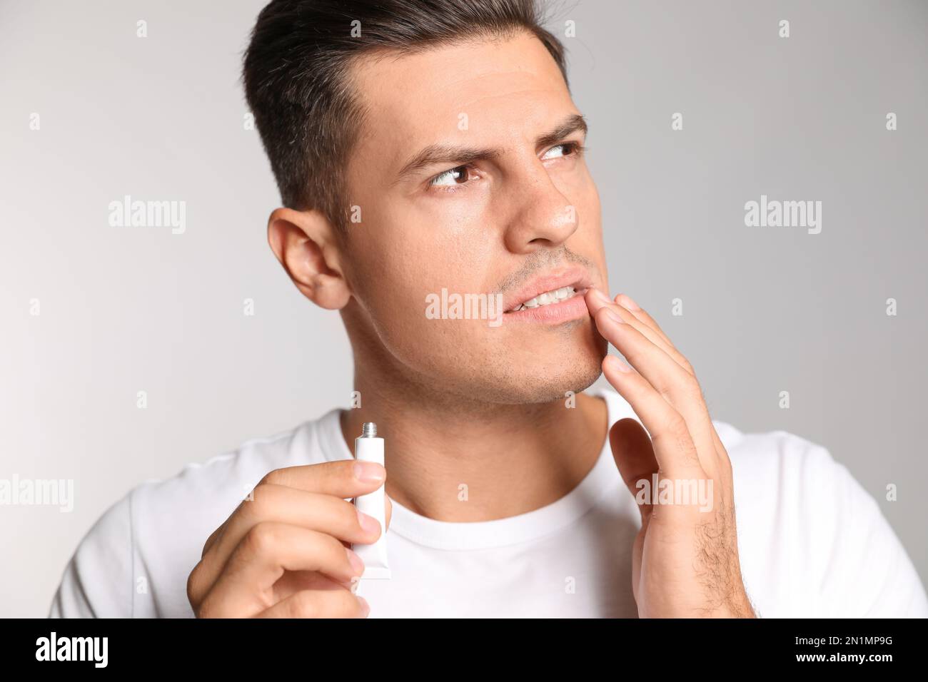 Man with herpes applying cream on lips against light grey background ...