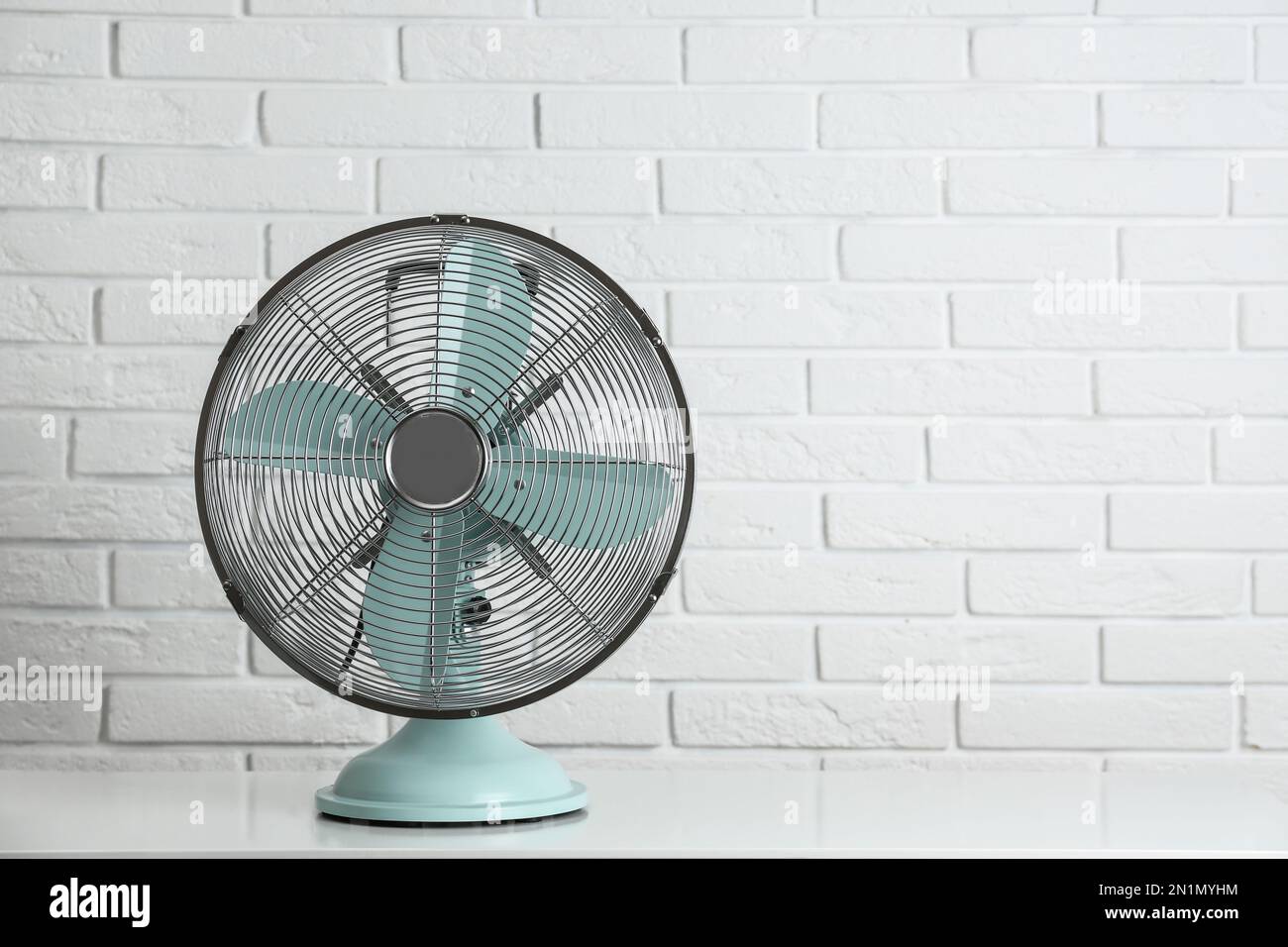 Electric fan on table near white brick wall, space for text. Summer ...