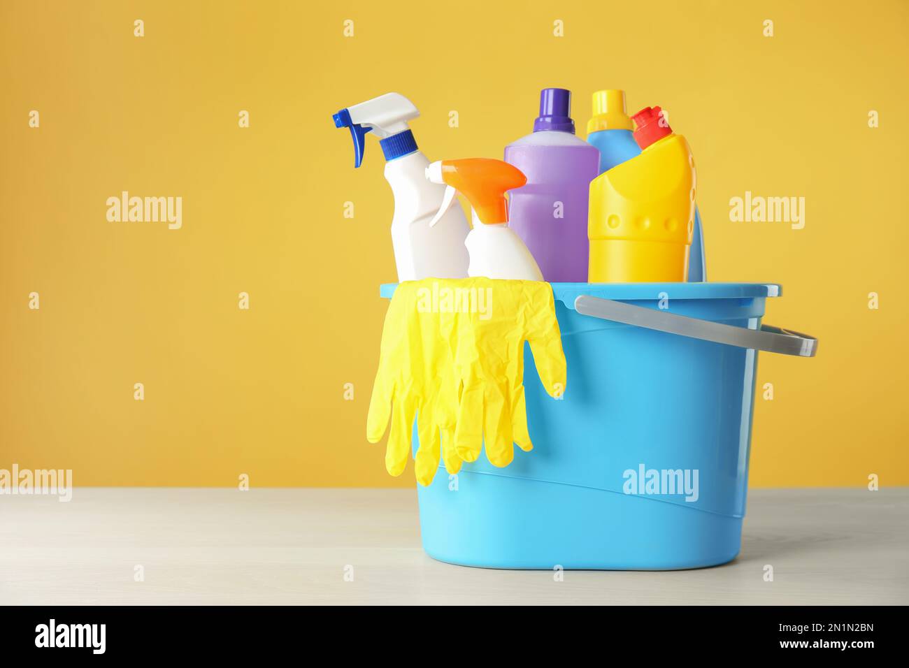Bucket with cleaning products and gloves on grey table. Space for text ...