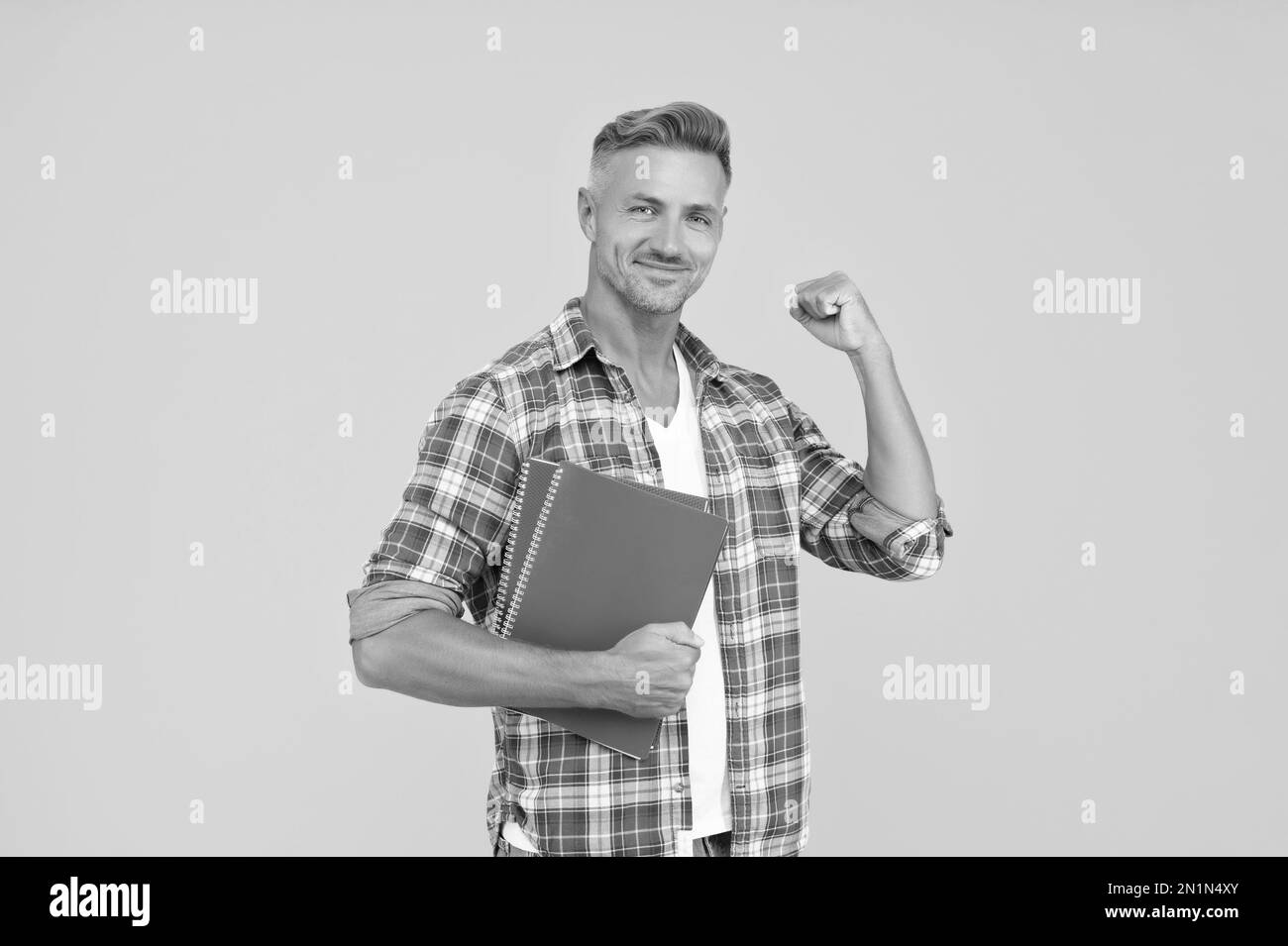 Excited guy teacher making winning gesture holding books yellow ...