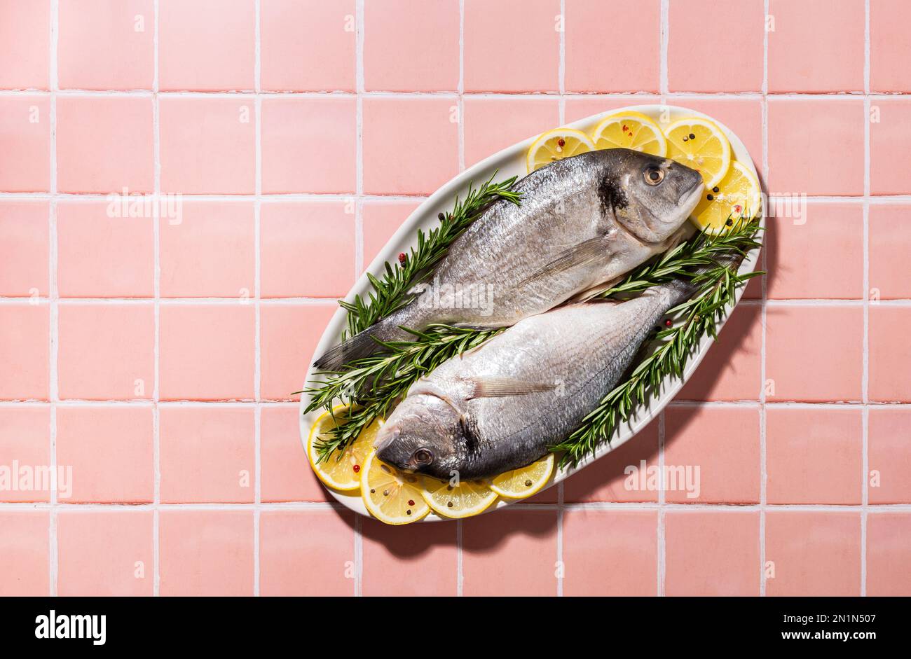 Dorada fish with lemon slices and rosemary sprigs in an oval dish on a ...