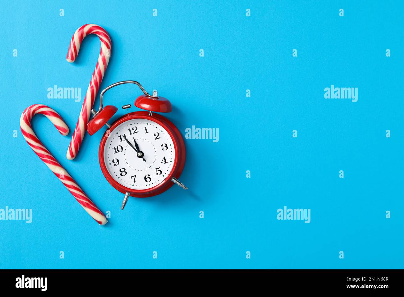 Alarm clock and candy canes on light blue background, flat lay with ...