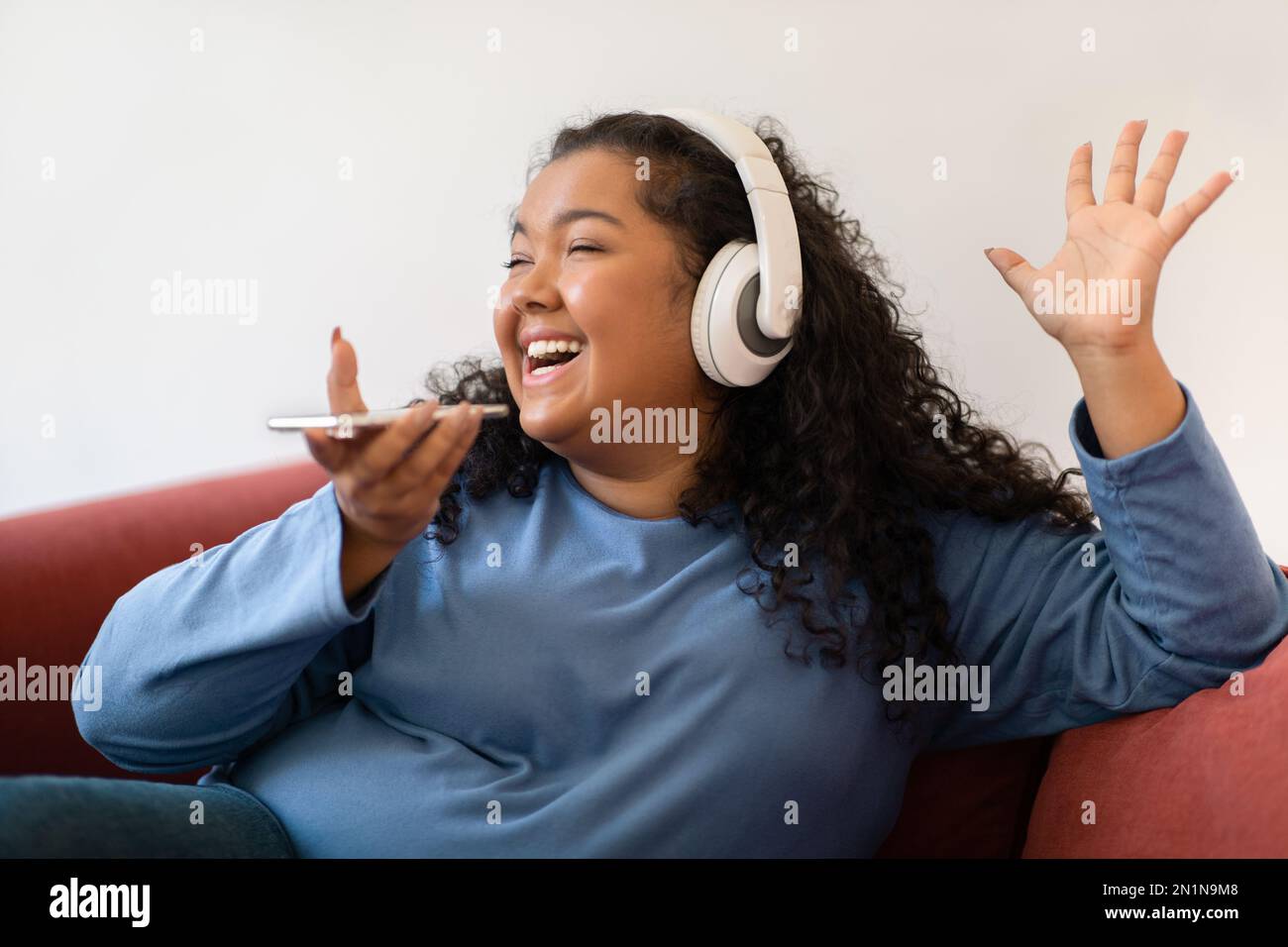 Happy hispanic lady sitting on sofa, singing songs, using phone Stock ...