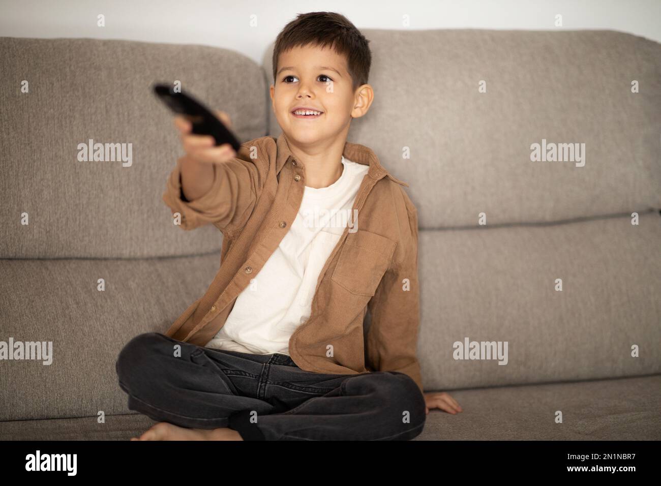 Cheerful caucasian little child with remote control switches channels ...