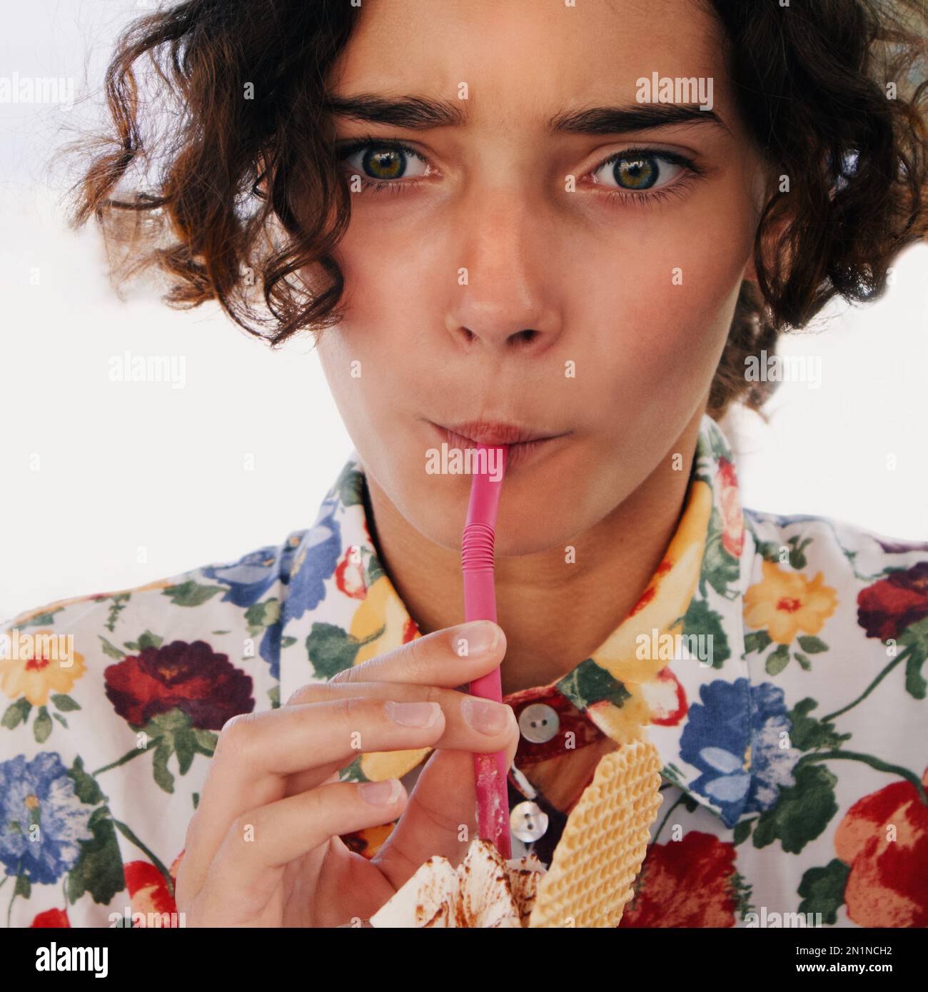 A young green-eye, curly-haired girl looks surprised while drinking a ...