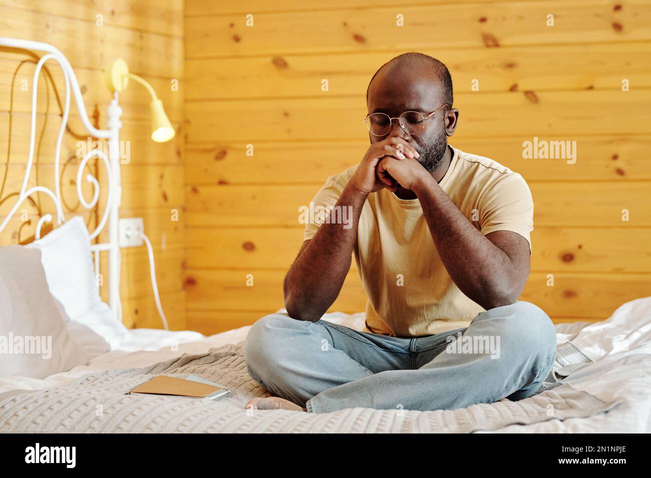 Young tense man in jeans and t-shirt keeping clenched hands by his face ...