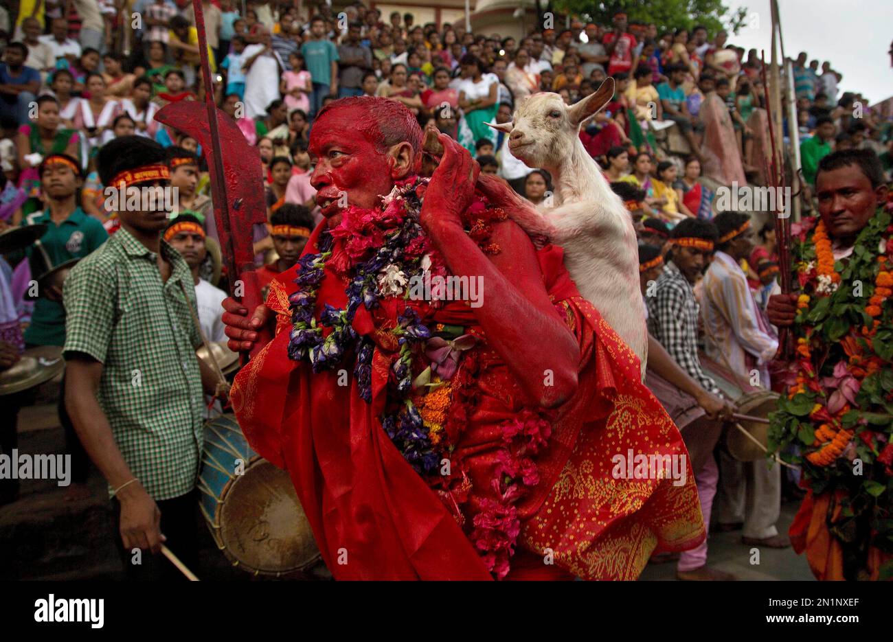 A Hindu priest, face smeared with color and sacrificial blood, carries ...