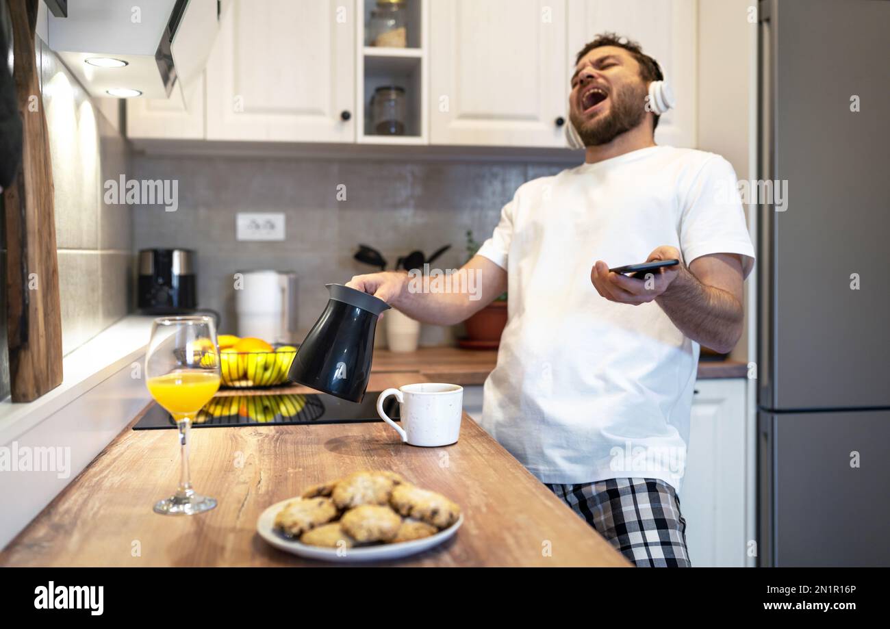 Man in headphones making coffee in morning listening music and singing ...