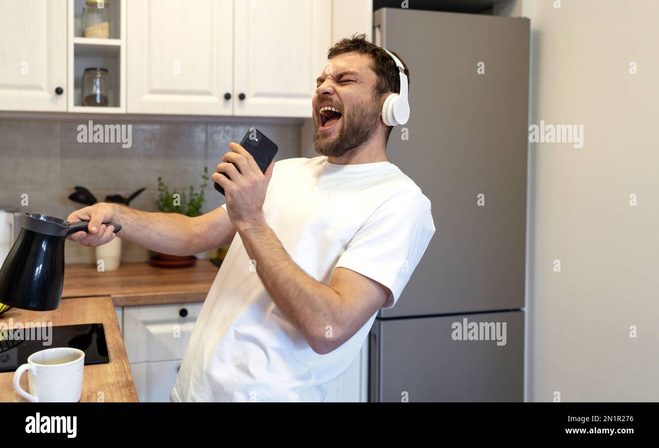 Man in headphones making coffee in morning listening music and singing ...