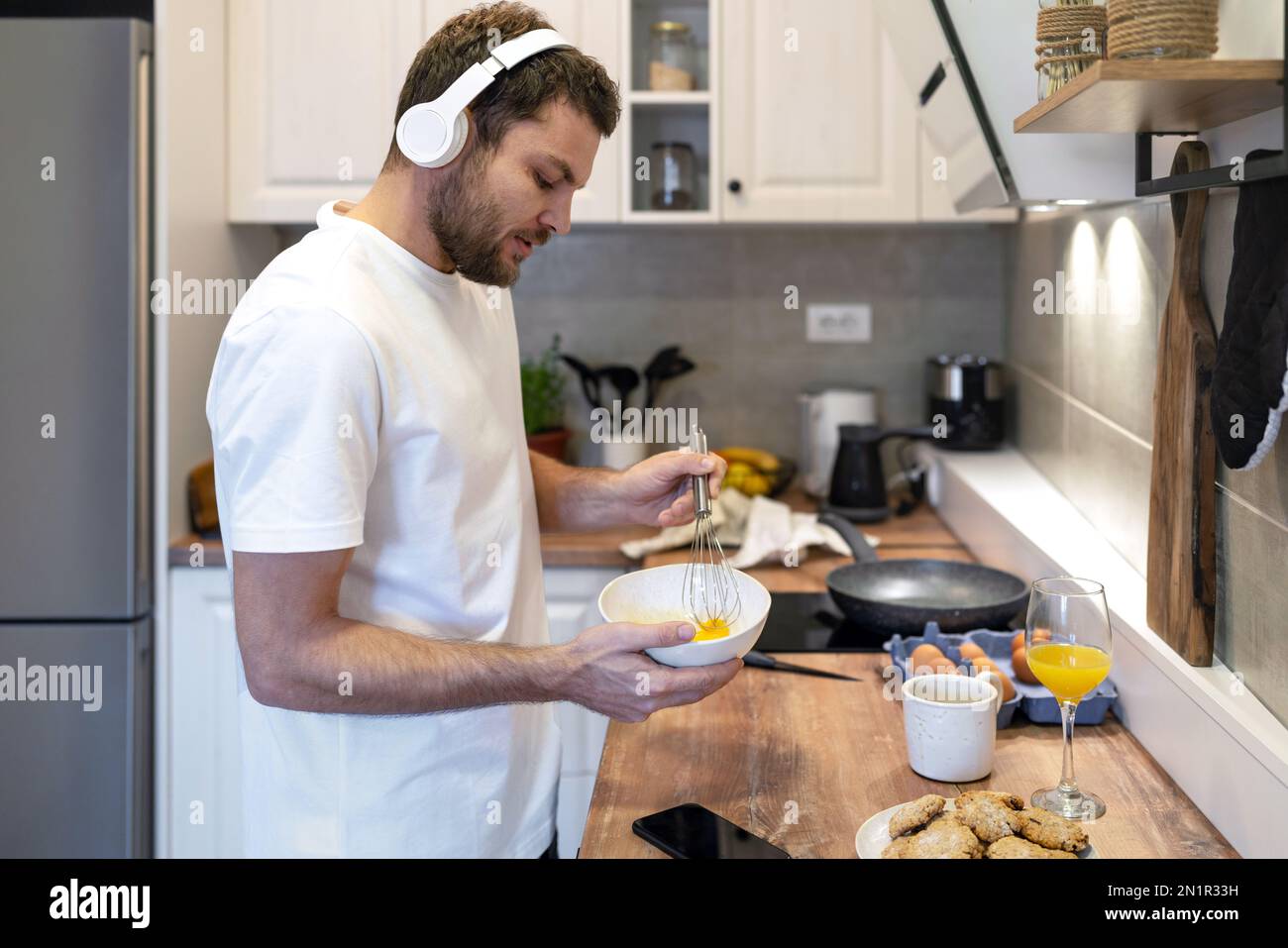 Man in white tee shirt and headphones standing in kitchen cooking ...