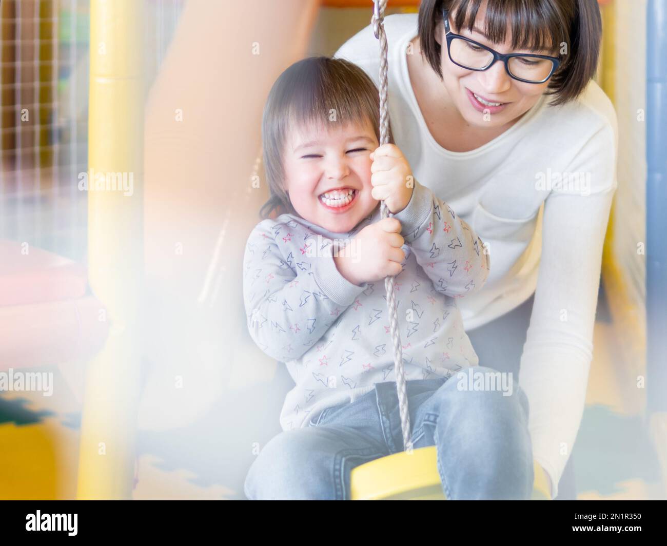 Toddler plays on rope swing with his mother or babysitter. Physical ...