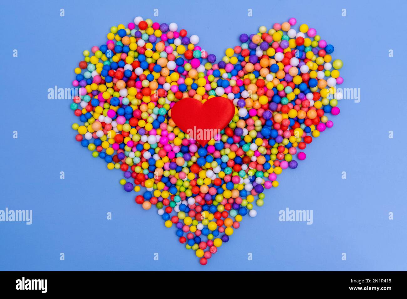 A large heart of bright multicolored round candies, dragees on a blue ...