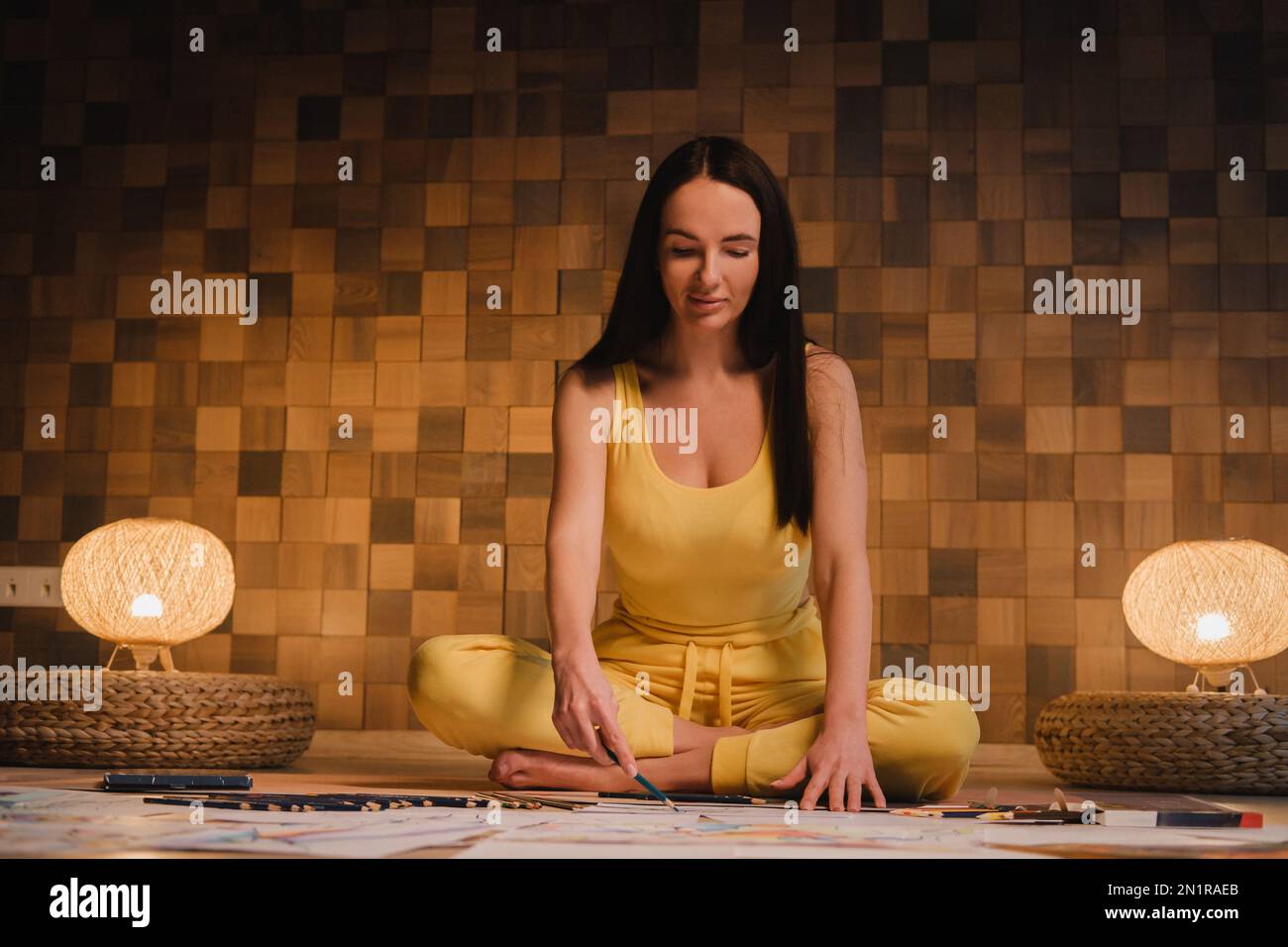 A girl in yellow clothes sitting in the Lotus position draws on paper ...