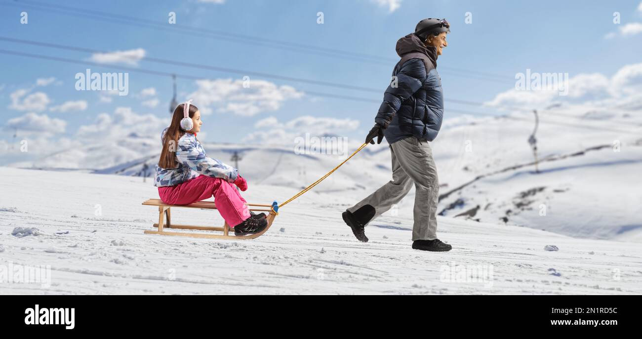 Man in winter clothes pulling a child with a sled on a mountain hill ...
