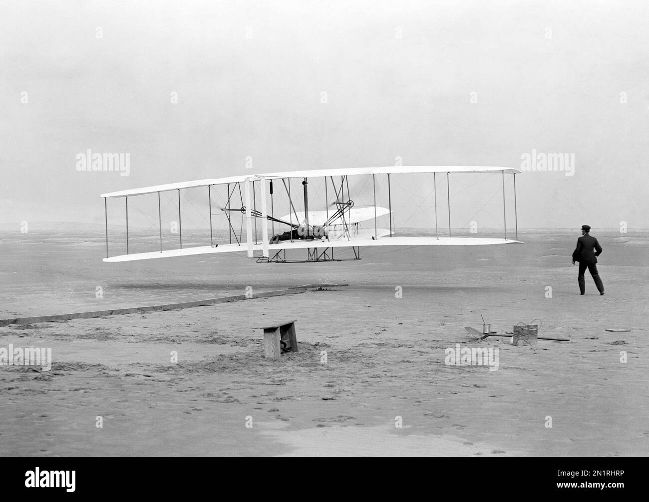 Orville Wright, lying at the controls on the lower wing, pilots the ...