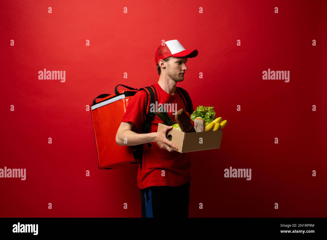 Side view delivery man in red uniform on a red background delivering ...