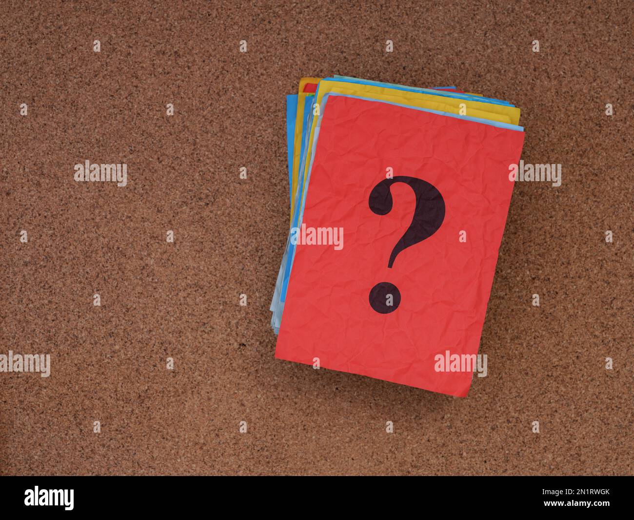 A stack of colorful paper notes with question marks on them on a cork ...