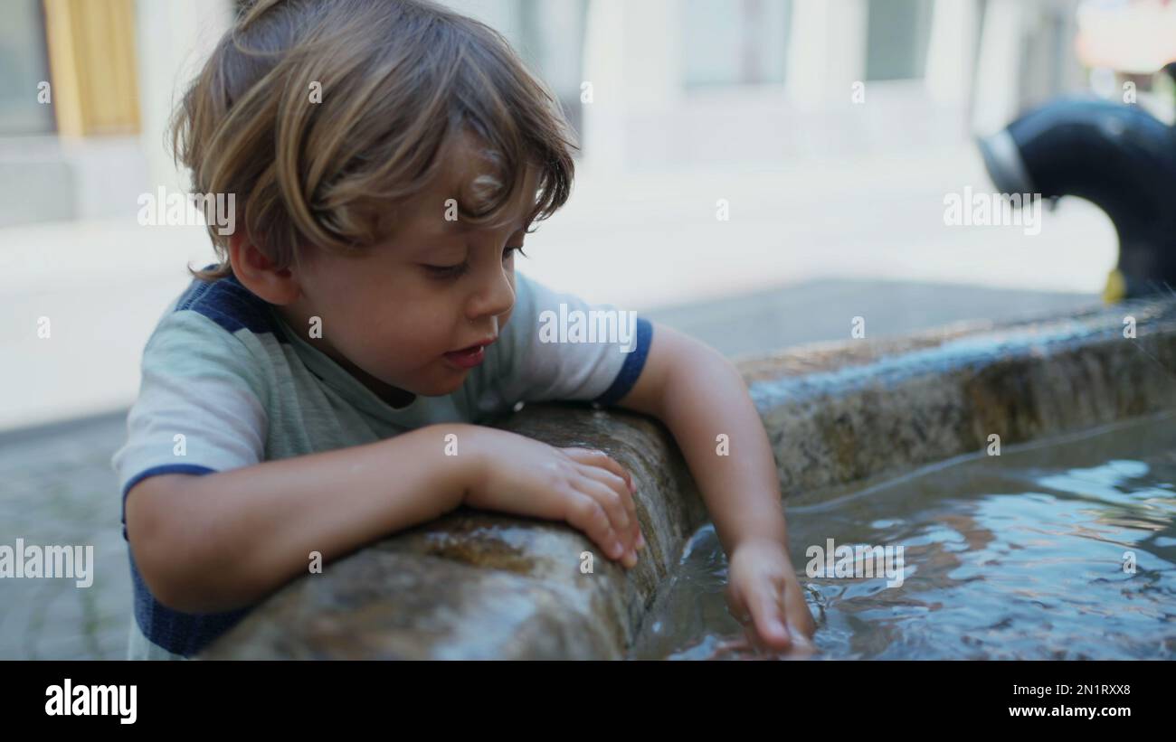 Child drinking clean water from public fountain in street. One small ...
