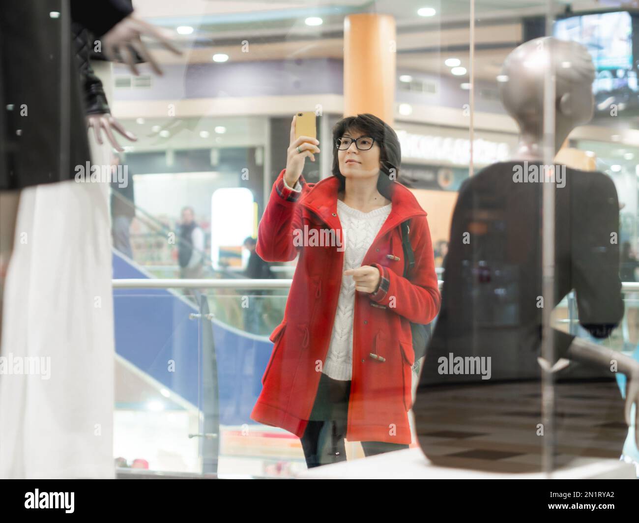 Woman takes photos of dummies in clothing store. Casual outfit hanging ...