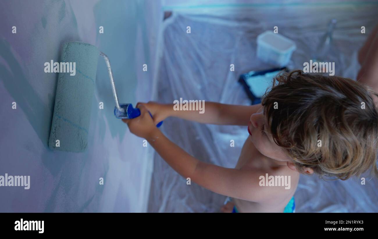Child painting wall with paint roller. Adorable small boy paints with ...