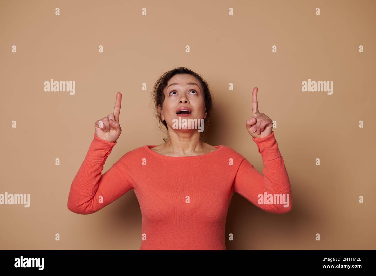 Beautiful Hispanic Surprised Woman Looking Up And Pointing Her Index