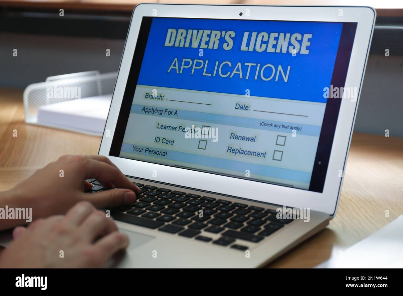 Woman using laptop to fill driver's license application form at table in office, closeup Stock ...