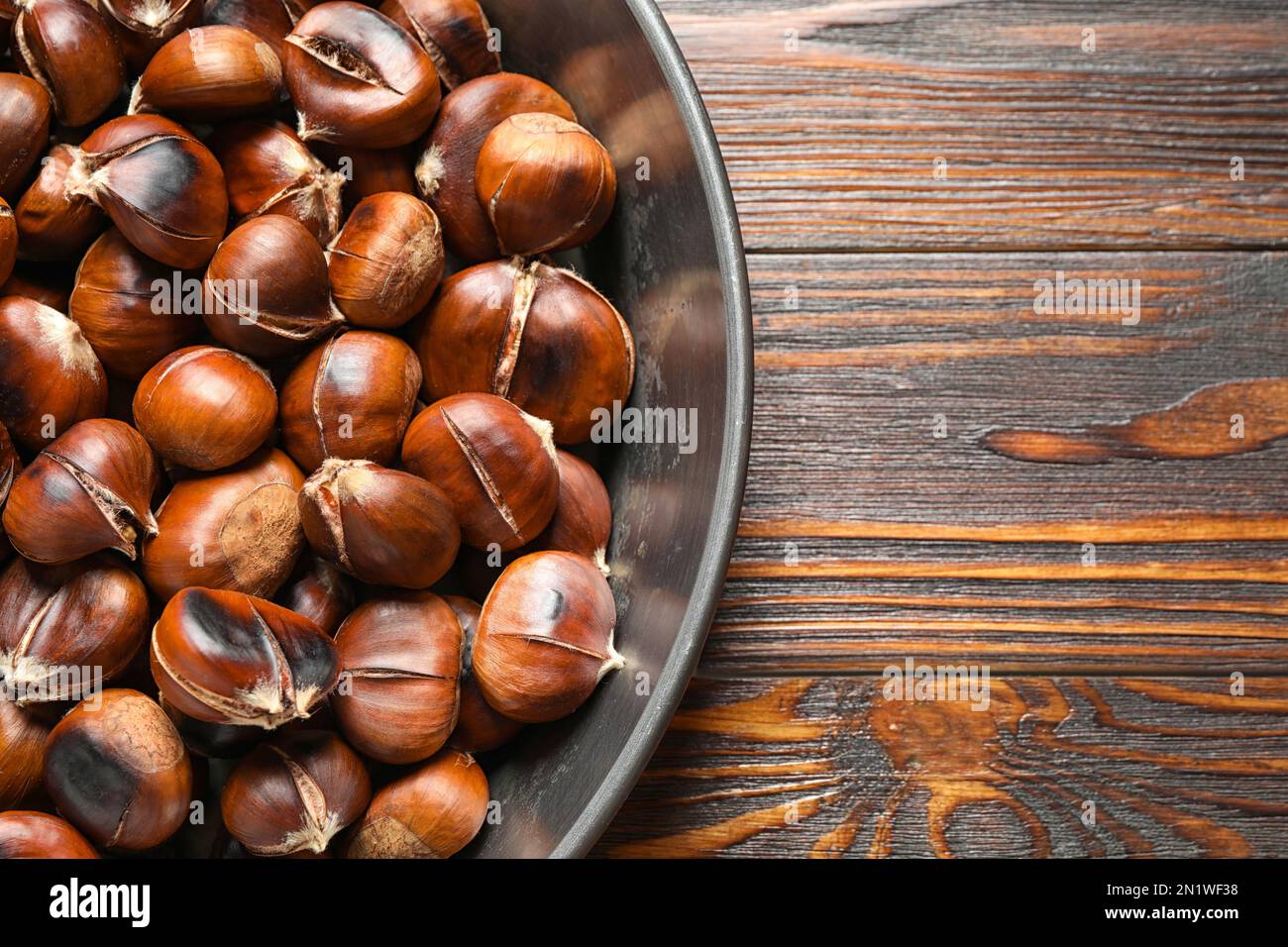 Delicious roasted edible chestnuts in frying pan on wooden table, top ...