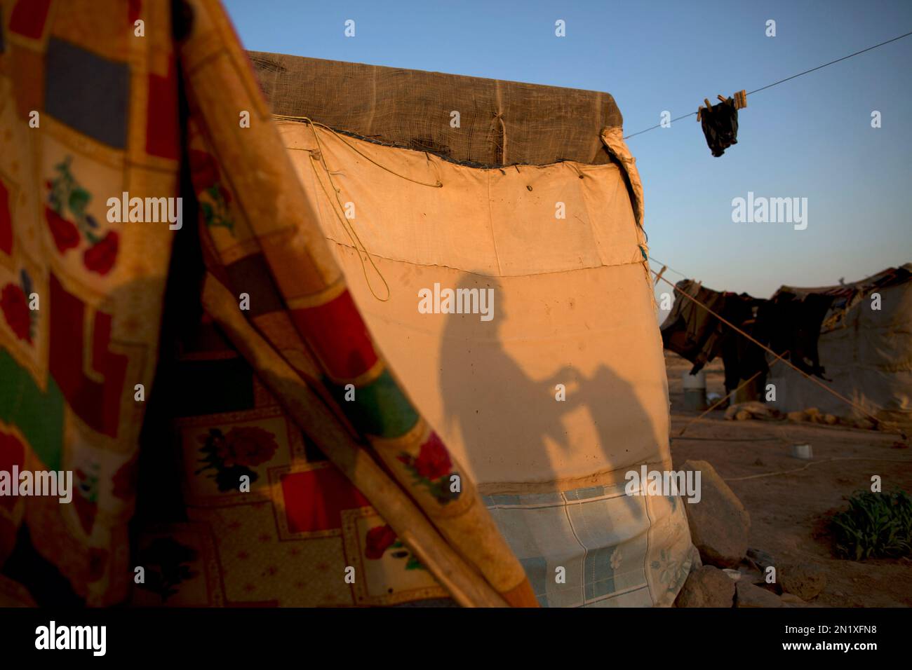 The shadow of a Syrian refugee woman hanging her laundry is cast on her ...