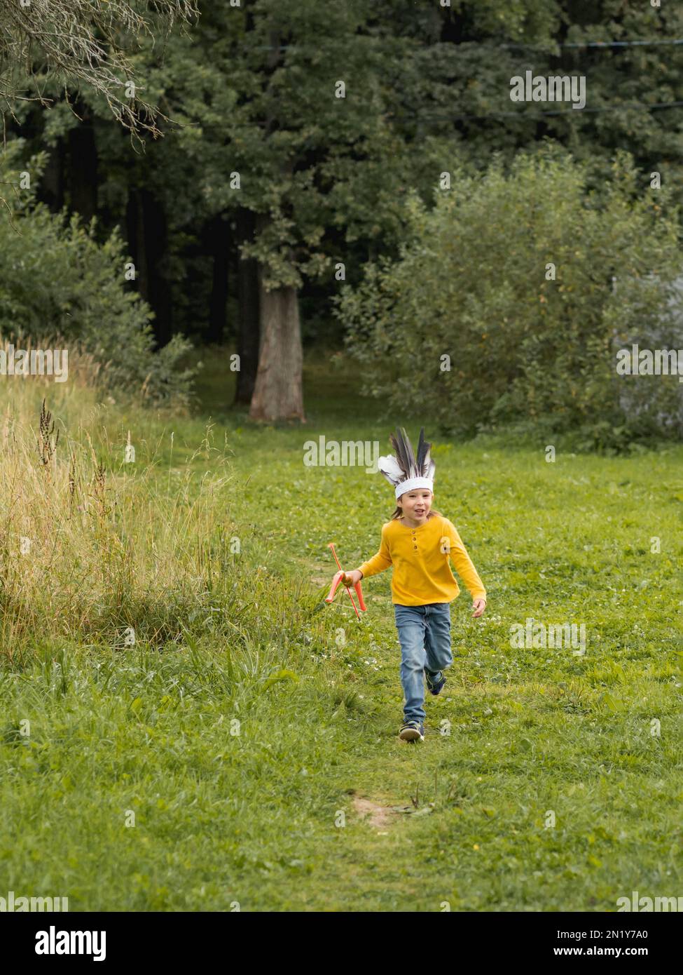 Running boy is playing American Indian on field. Kid has handmade ...