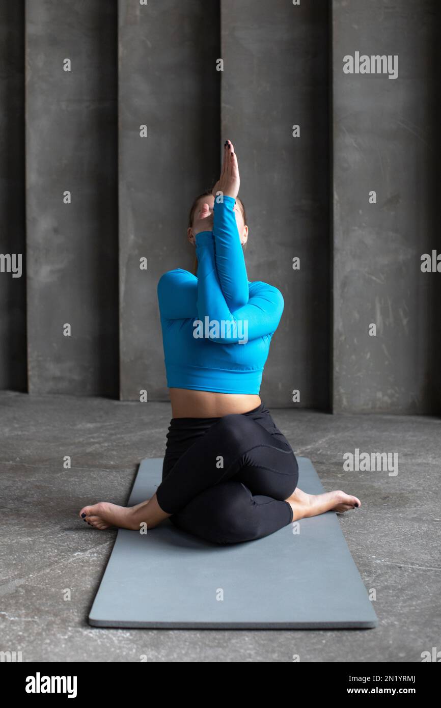 A woman practices yoga while sitting on a mat with her legs crossed and ...