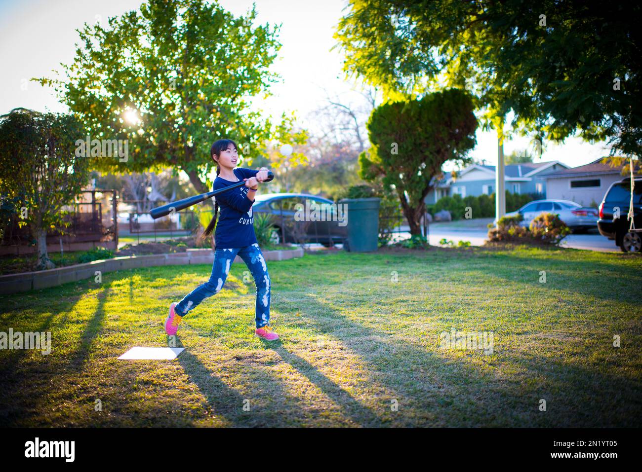 Young asian girl hitting baseball in front yard during sunset Stock ...