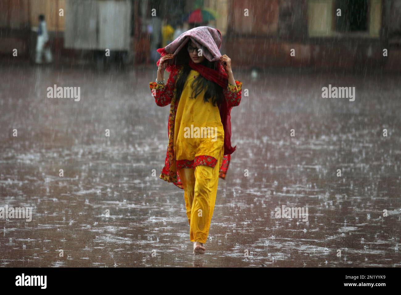 A Pakistani girl covers her head with a prayer mat to shelter from rain ...