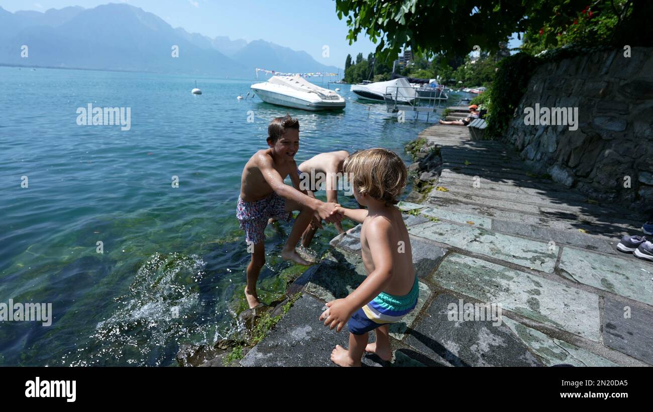 Little boy helping older brother get out of water. Baby sibling giving ...