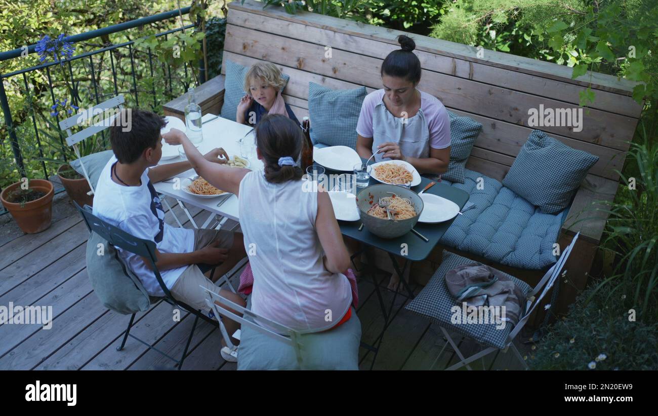 People eating lunch at house wooden patio outdoors. Children and two ...