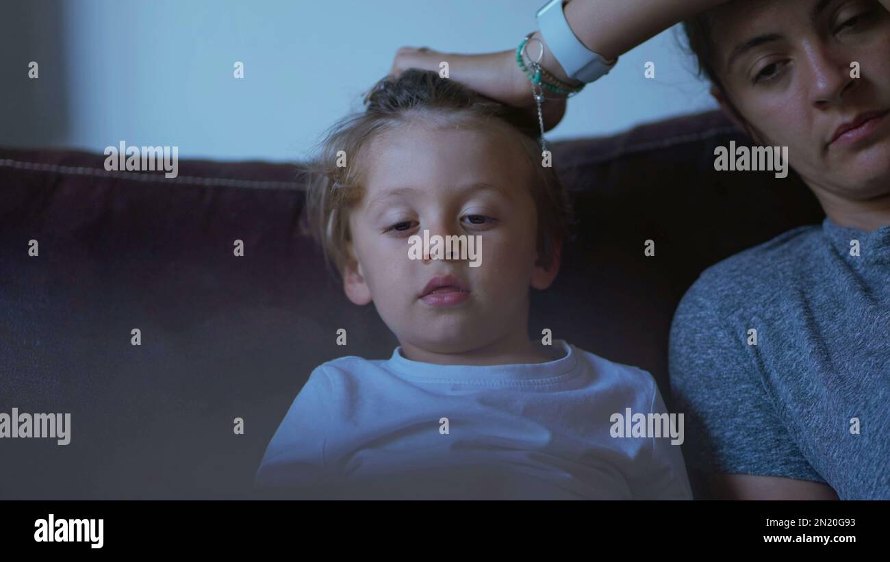 Mother caressing child hair watching movie together sitting on sofa ...