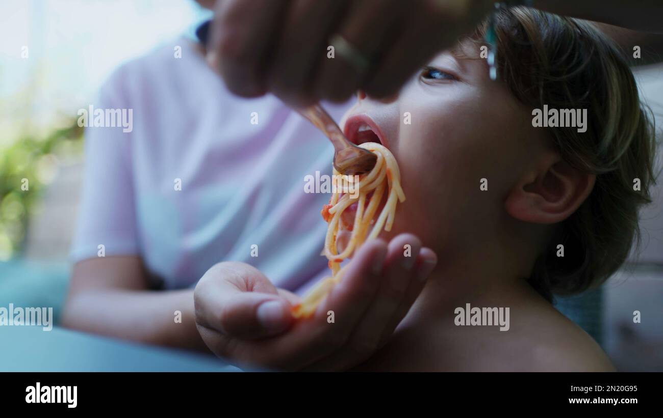 Mother feeding pasta to little boy. Child eating spaghetti for lunch ...
