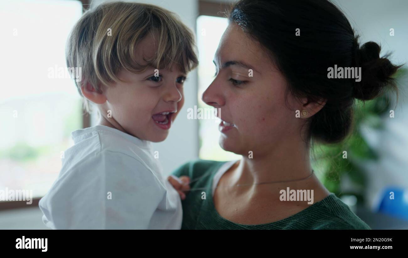 Mother holding child in arms kissing and embracing kid. Candid mom showing love affection to ...